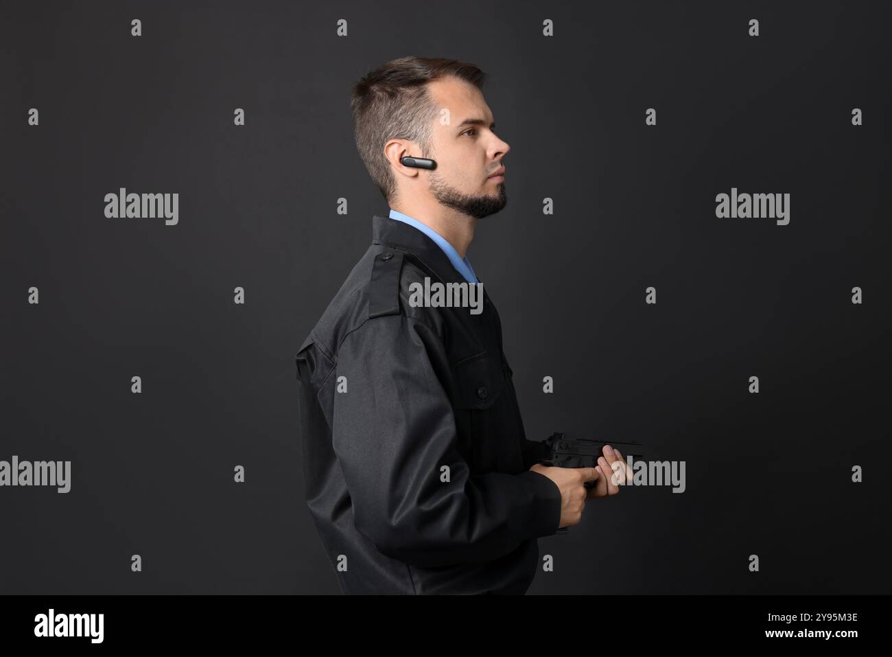 Security guard in uniform with earpiece and gun on black background ...