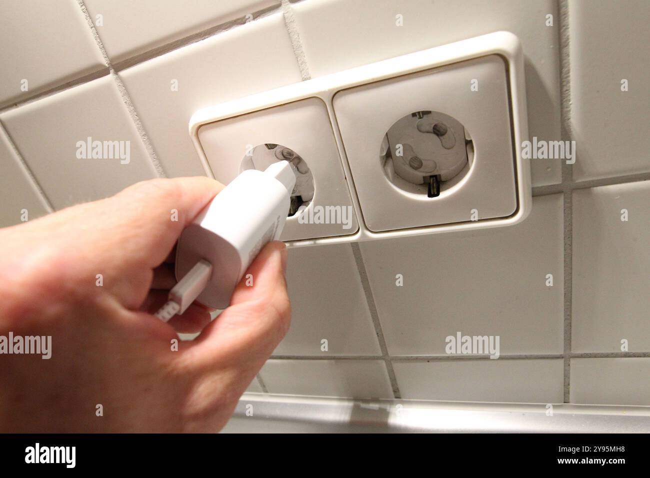 Ein Mann steckt ein Handy-Lagdegerät in eine Steckdose. Symbolbild ...