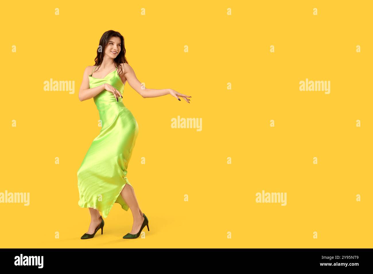 Happy young woman in stylish green dress dancing on yellow background ...
