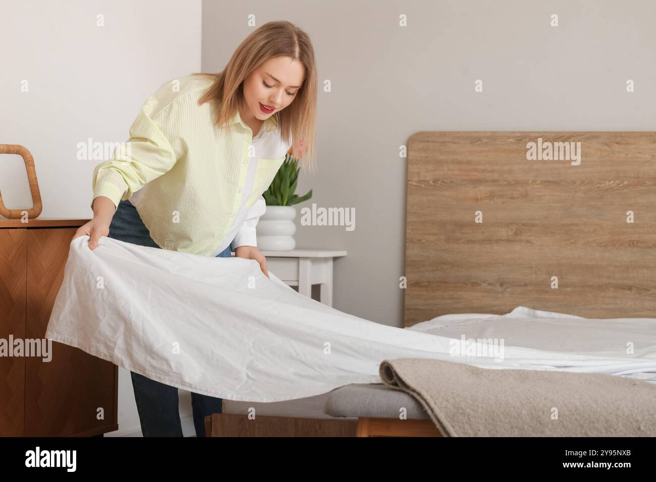 Pretty young woman making bed in bedroom Stock Photo - Alamy