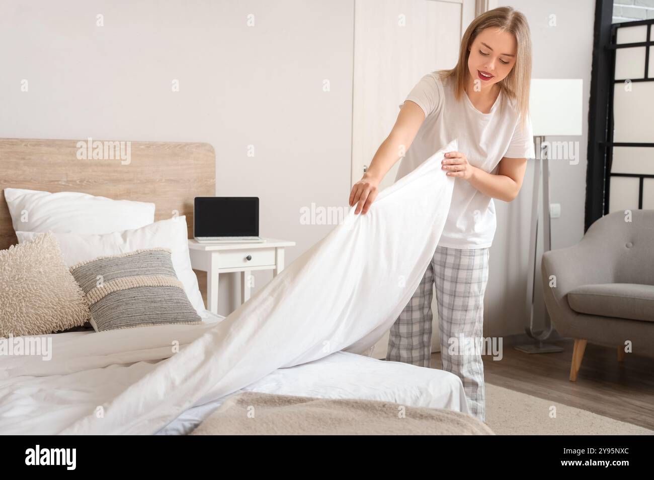 Pretty young woman making bed in bedroom Stock Photo - Alamy