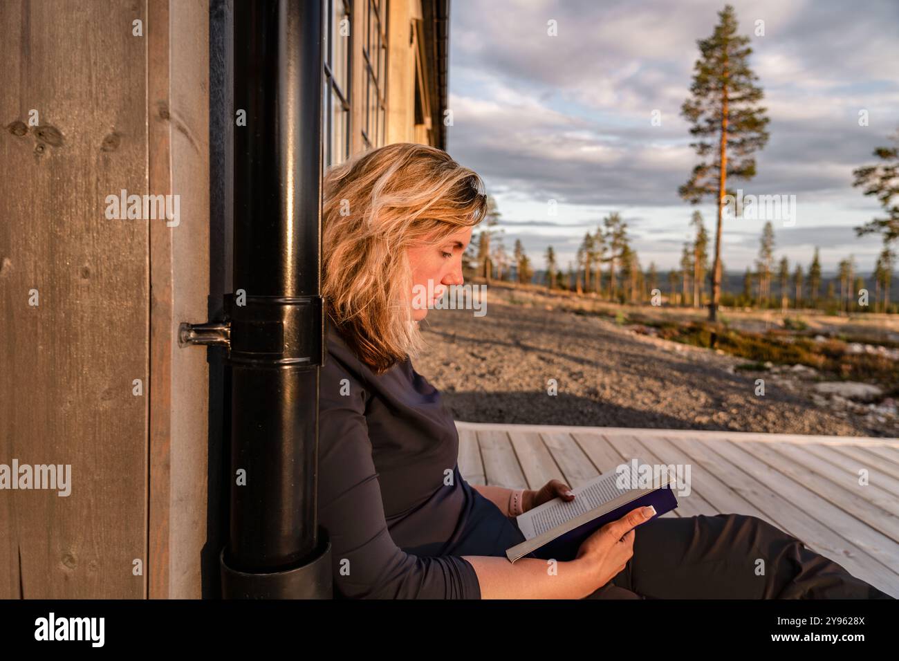 A beautiful woman sits peacefully on a deck, reading a book with ...