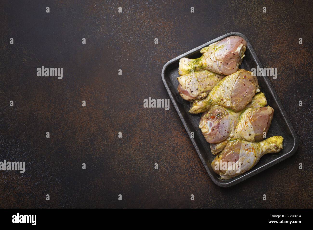 Raw uncooked chicken legs in green marinade with seasonings in black ...