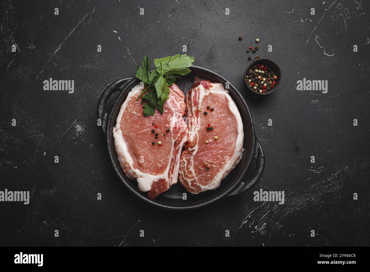 Cut raw meat pork steaks with seasonings in black cast iron pan, dark ...