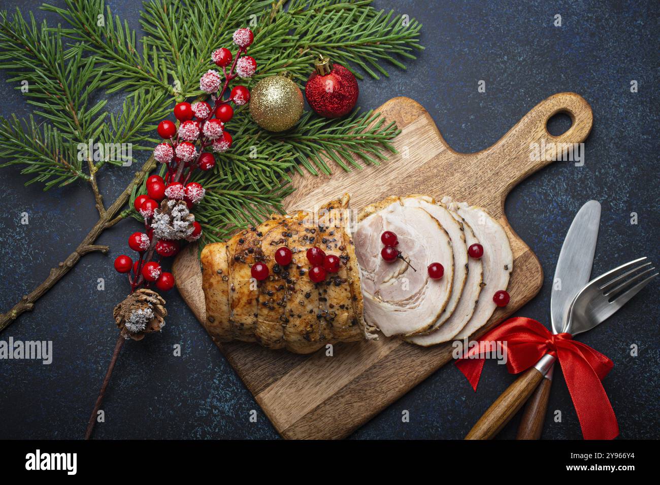 Christmas baked ham sliced with red berries and festive decorations on ...