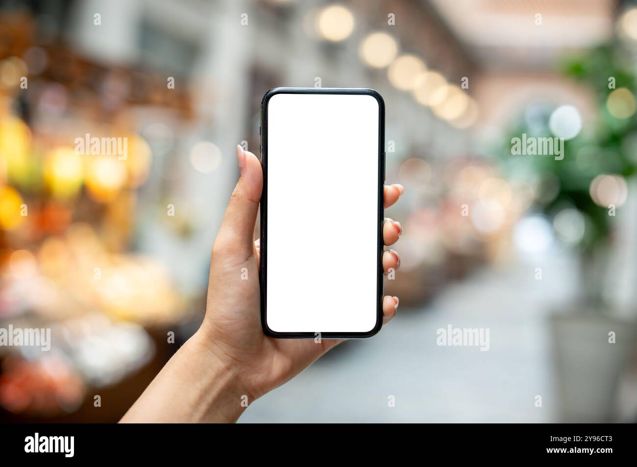 A close-up of a woman's hand holding a smartphone with a white screen ...