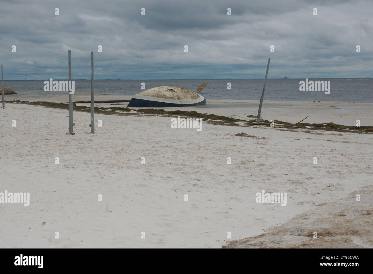 Blue and white Beached sailboat turned on its side on beach. After ...