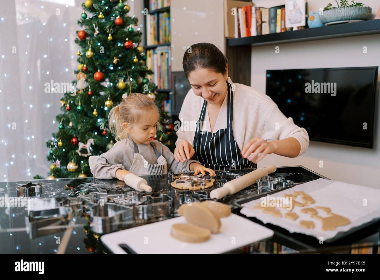 Smiling mother watching little girl pressing cookie cutters on rolled ...