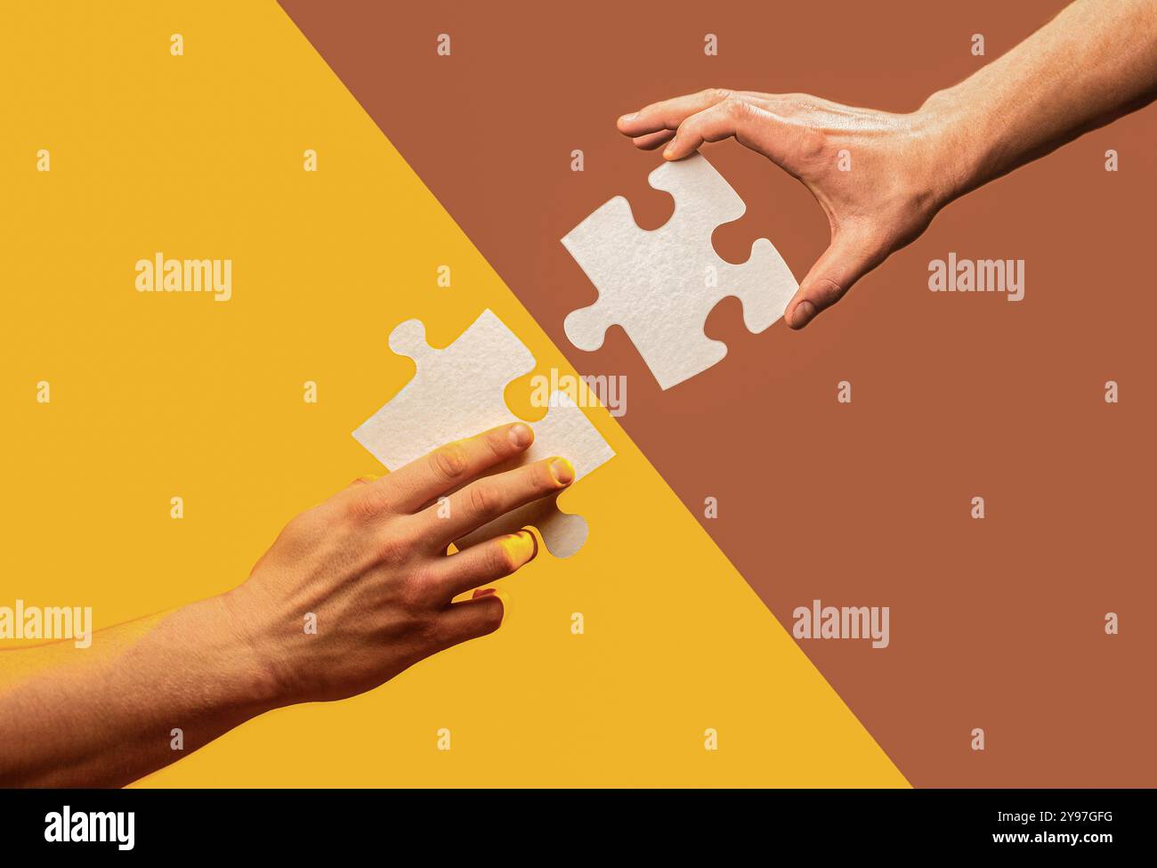 Two puzzle pieces are interlocking on coloured background. Human hands ...