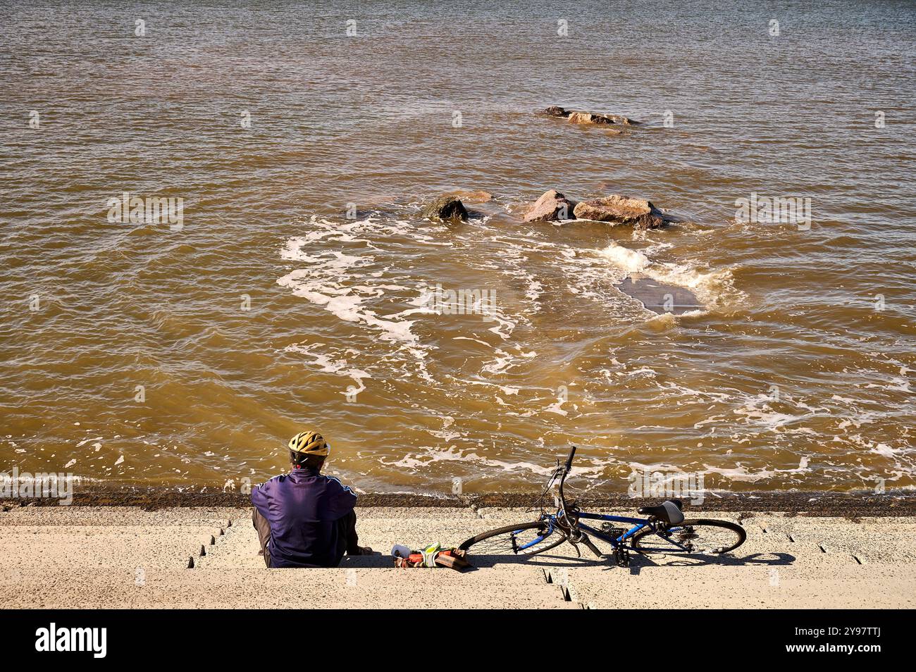 Cyclist resting on steps of seawall at high tide,UK Stock Photo - Alamy