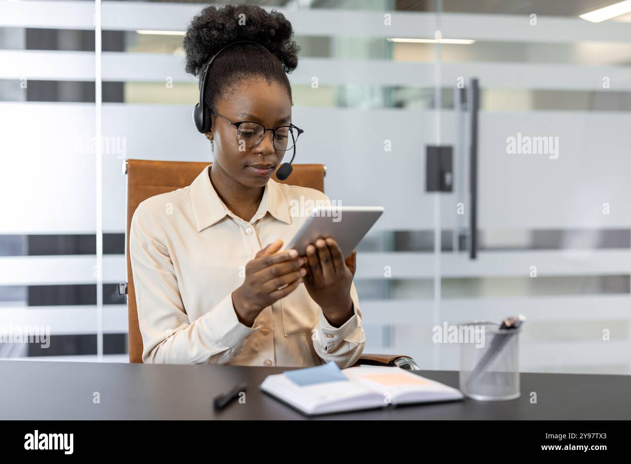Professional woman engaged with tablet in office while wearing headset ...