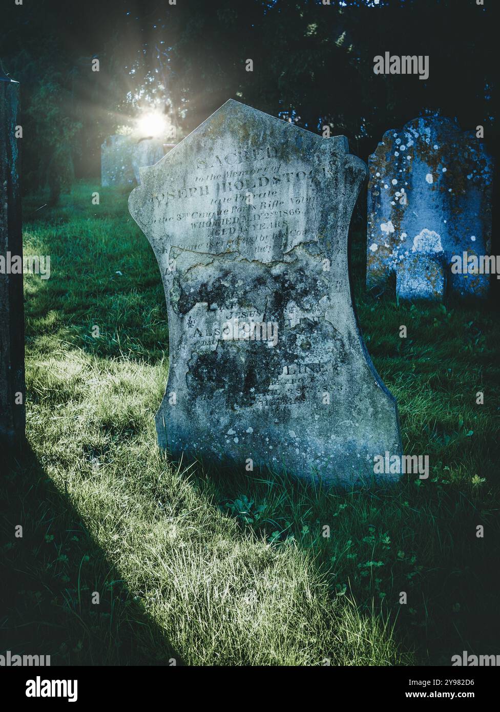 A sombre and twisted gravestone, illuminated by beams of light creating ...