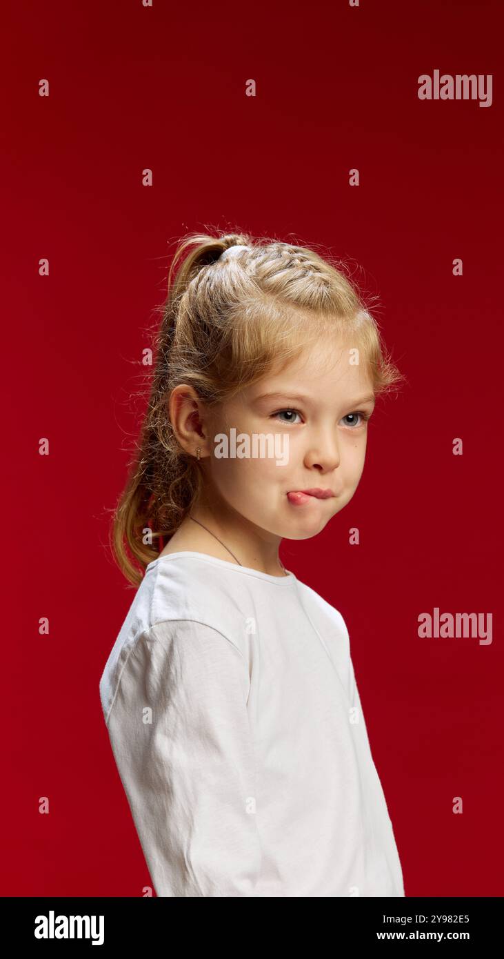 Little girl playfully puffs cheeks, biting her lower lip while looking ...