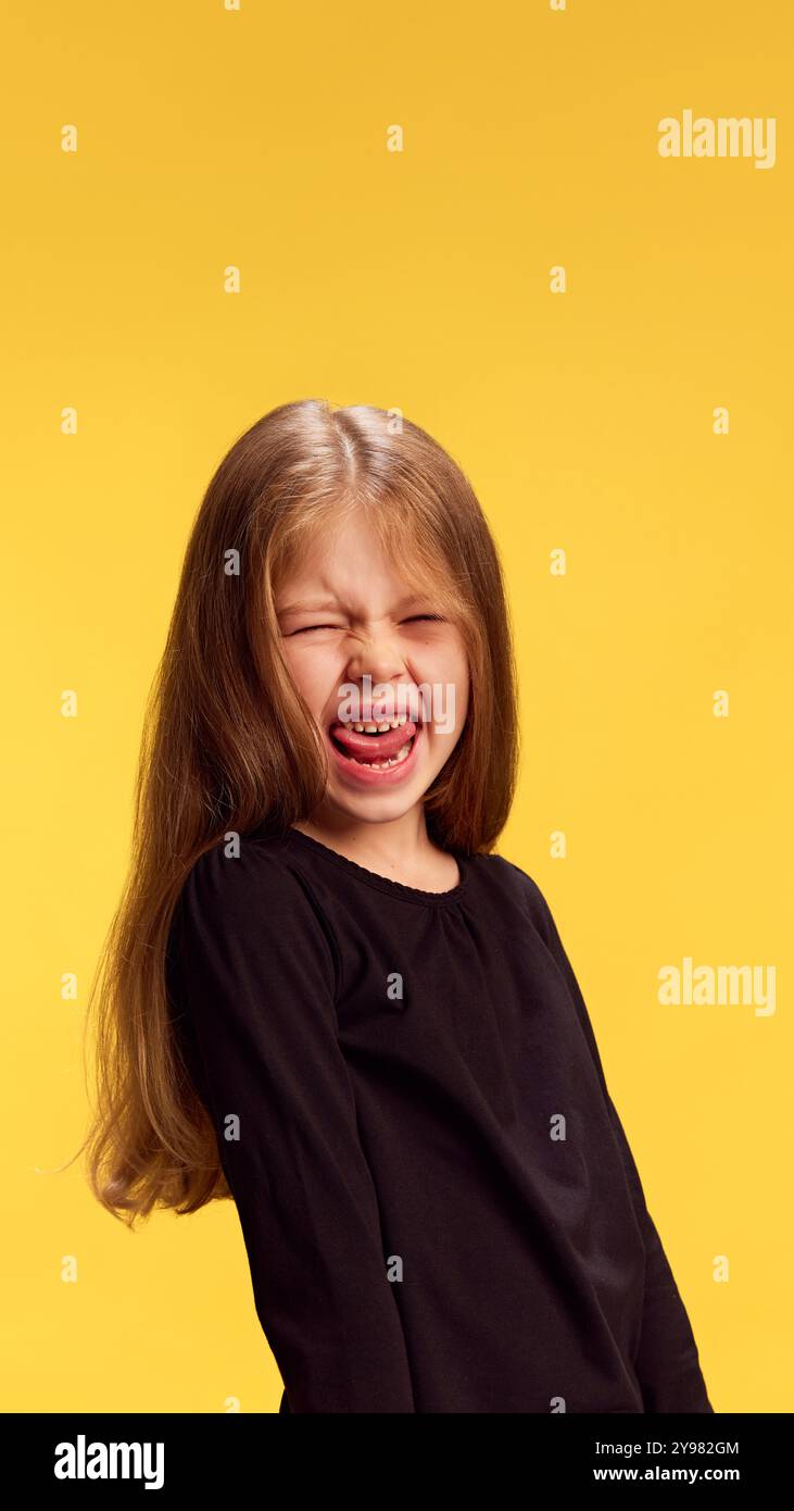 Little, schoolgirl sticks out her tongue, squinting her eyes in ...