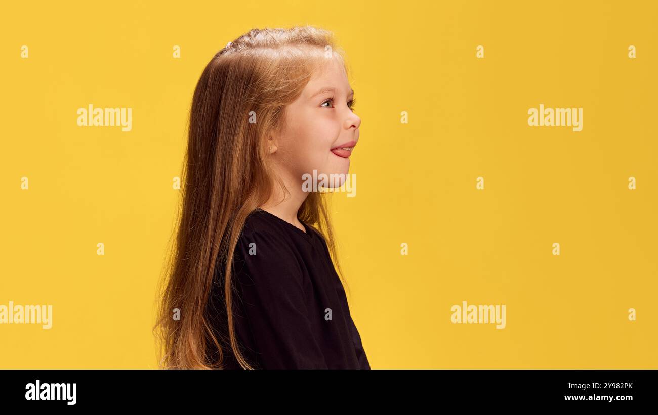 Side profile of little girl sticking her tongue out, smiling slightly ...