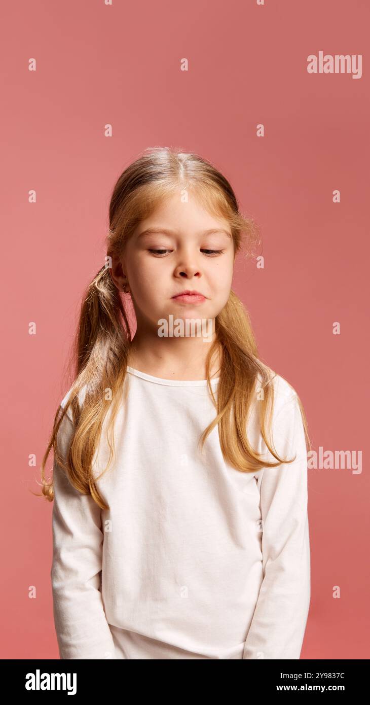 Little girl with blonde hair in pigtails and white shirt looks down ...