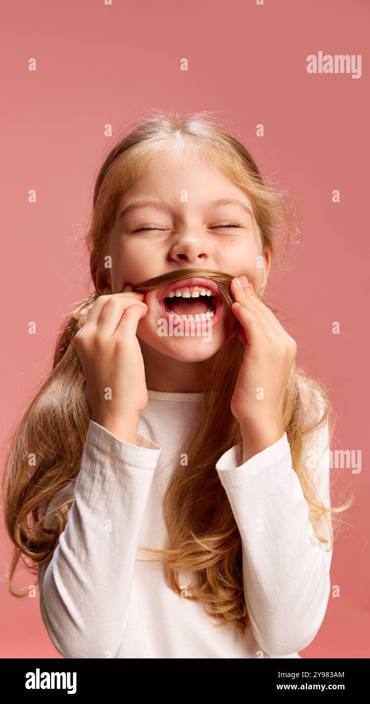 Girl with light hair holding her hair above her lips to mimic mustache and laughing, giving ...