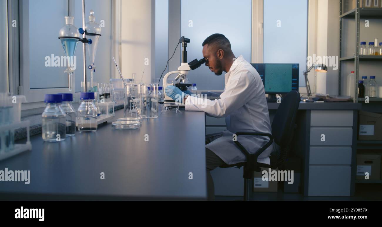 Medical science lab: African American male microbiologist looks under ...