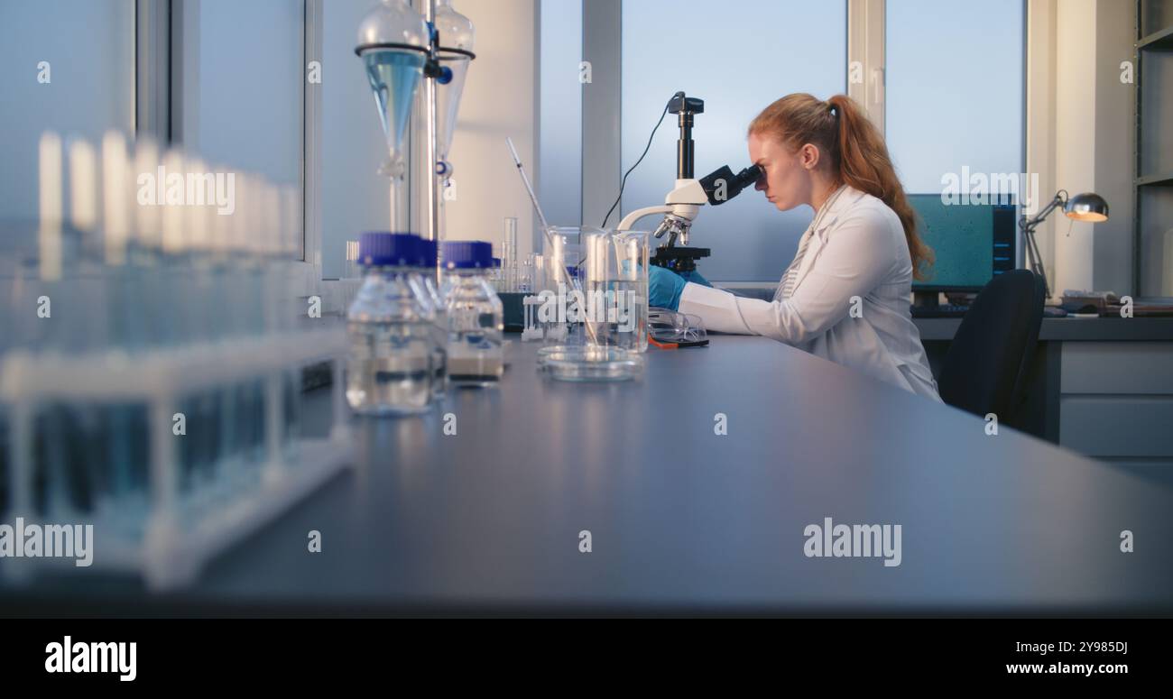 Beautiful female microbiologist in white coat working with microscope ...
