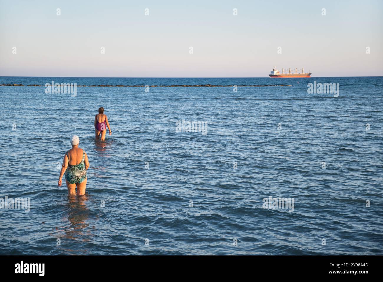 two elderly women entering the waters in Voroklini beach, larnaca just ...