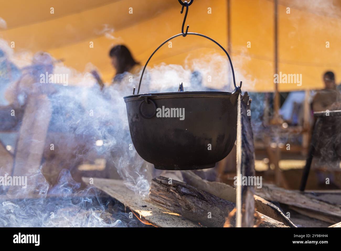 Black cauldron is hanging over a burning campfire, preparing a meal for ...