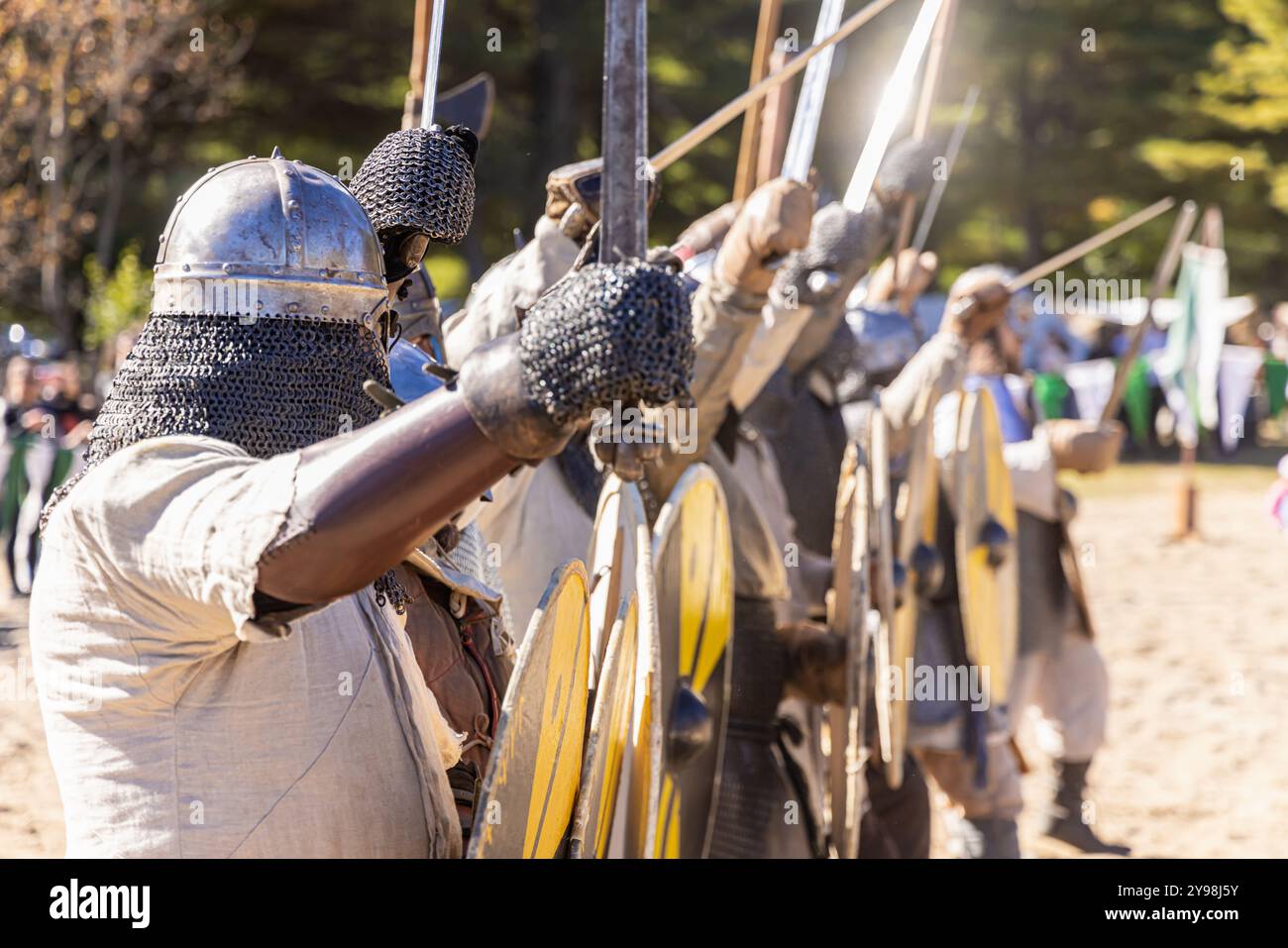Medieval reenactors wearing chainmail armor and holding swords and shields are lined up ...