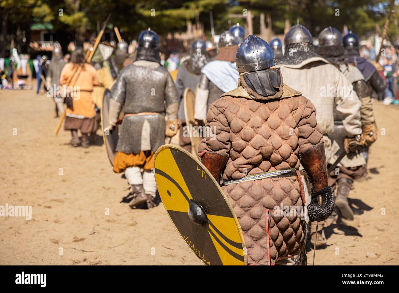 Group of medieval reenactors wearing helmets and carrying shields marching across battlefield ...