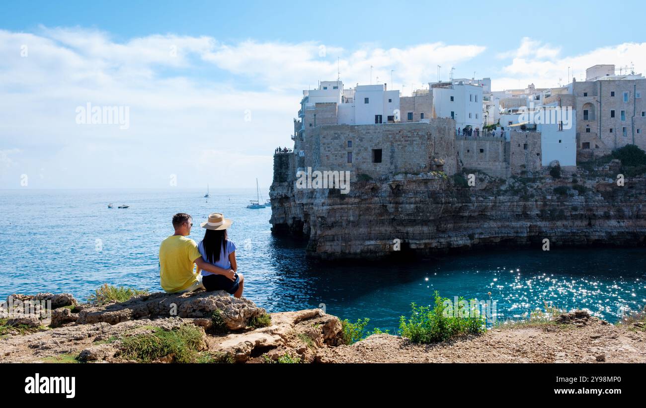 A couple relaxes on a rocky ledge, gazing at the stunning coastal ...