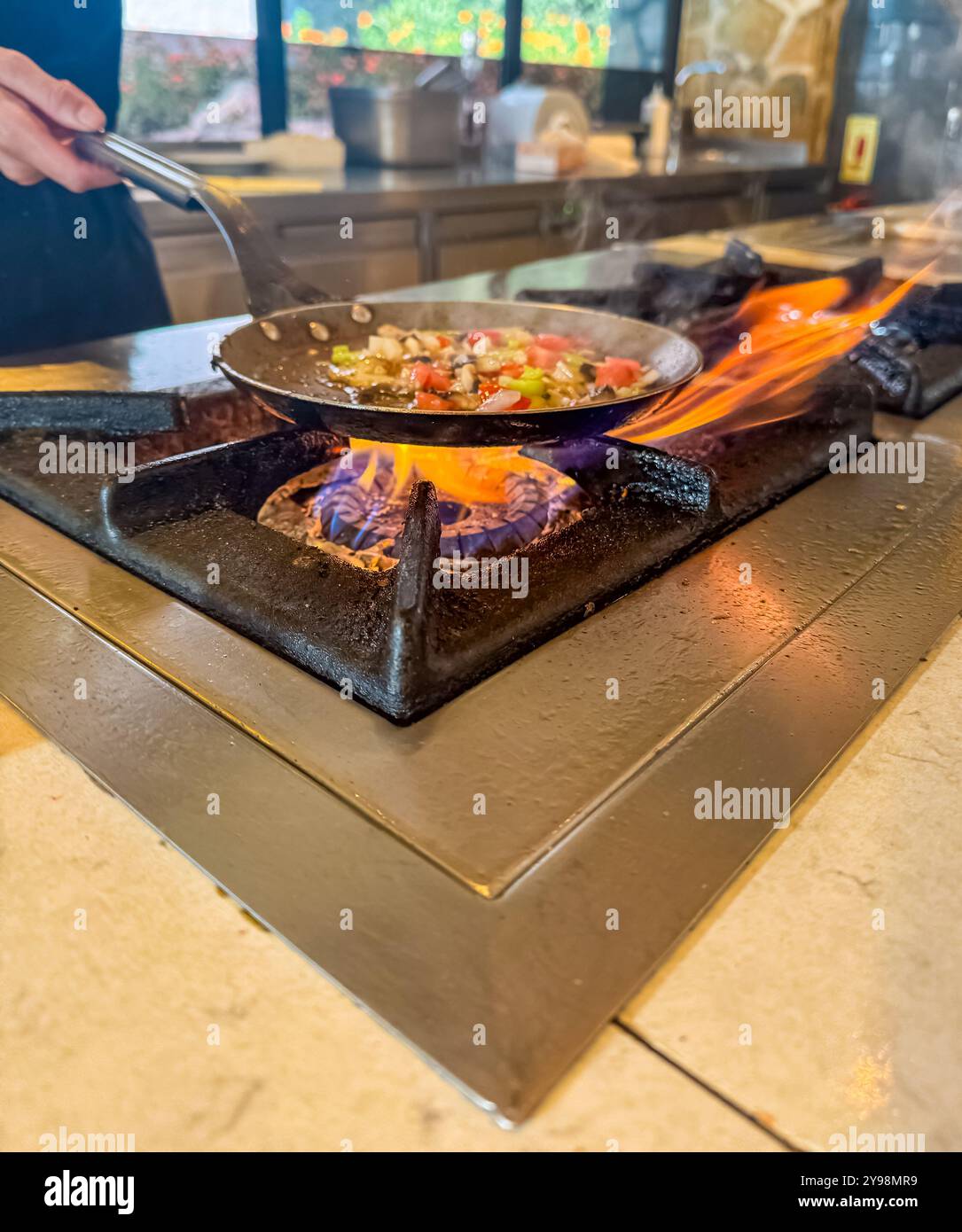 Chef cooking vegetables on a gas stove in a kitchen using a saute pan ...