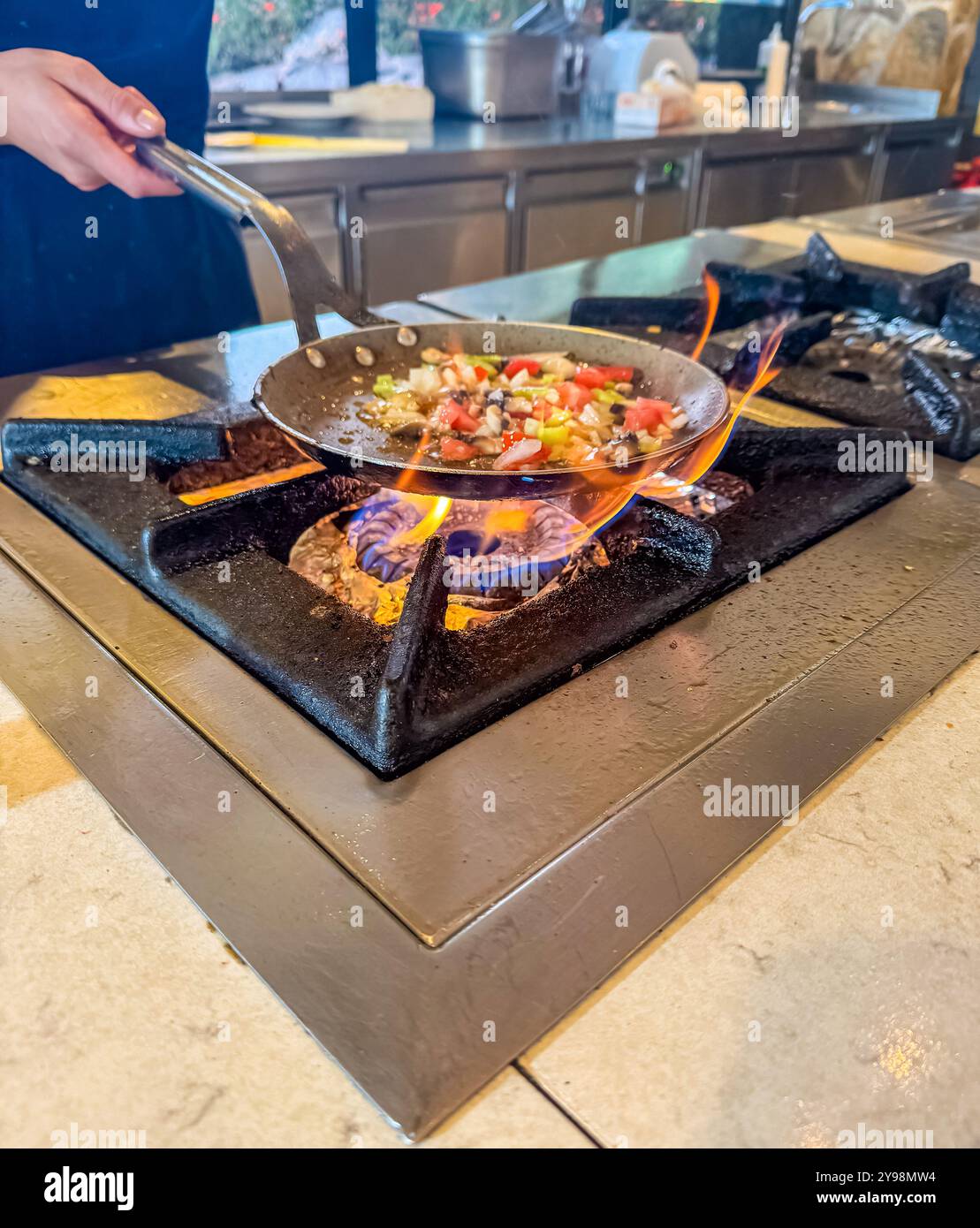 Chef cooking vegetables on a gas stove in a kitchen using a saute pan ...