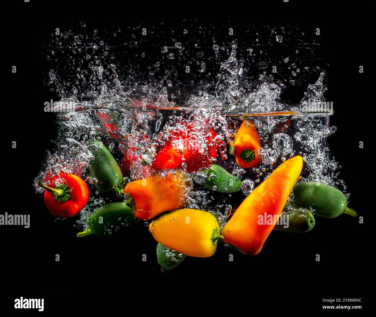 Red, yellow, orange and green chilli peppers splashing into water on a ...