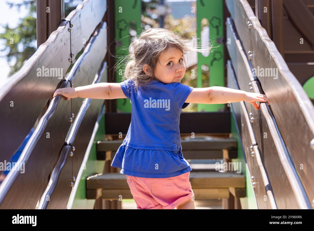 Young girl walking up a wooden ramp on a playground, looking back over ...