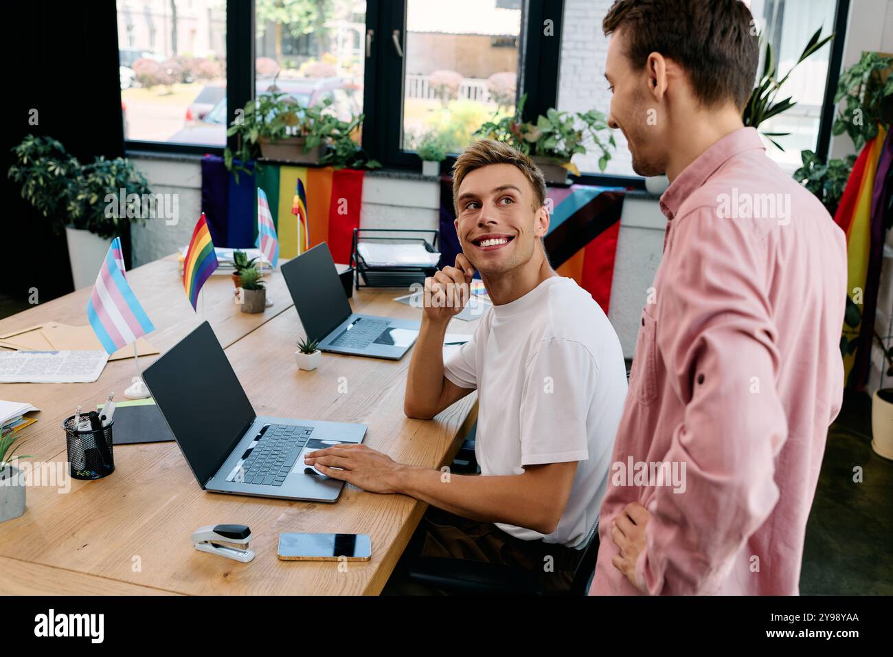 Two happy men engage in a lively discussion, surrounded by pride flags ...