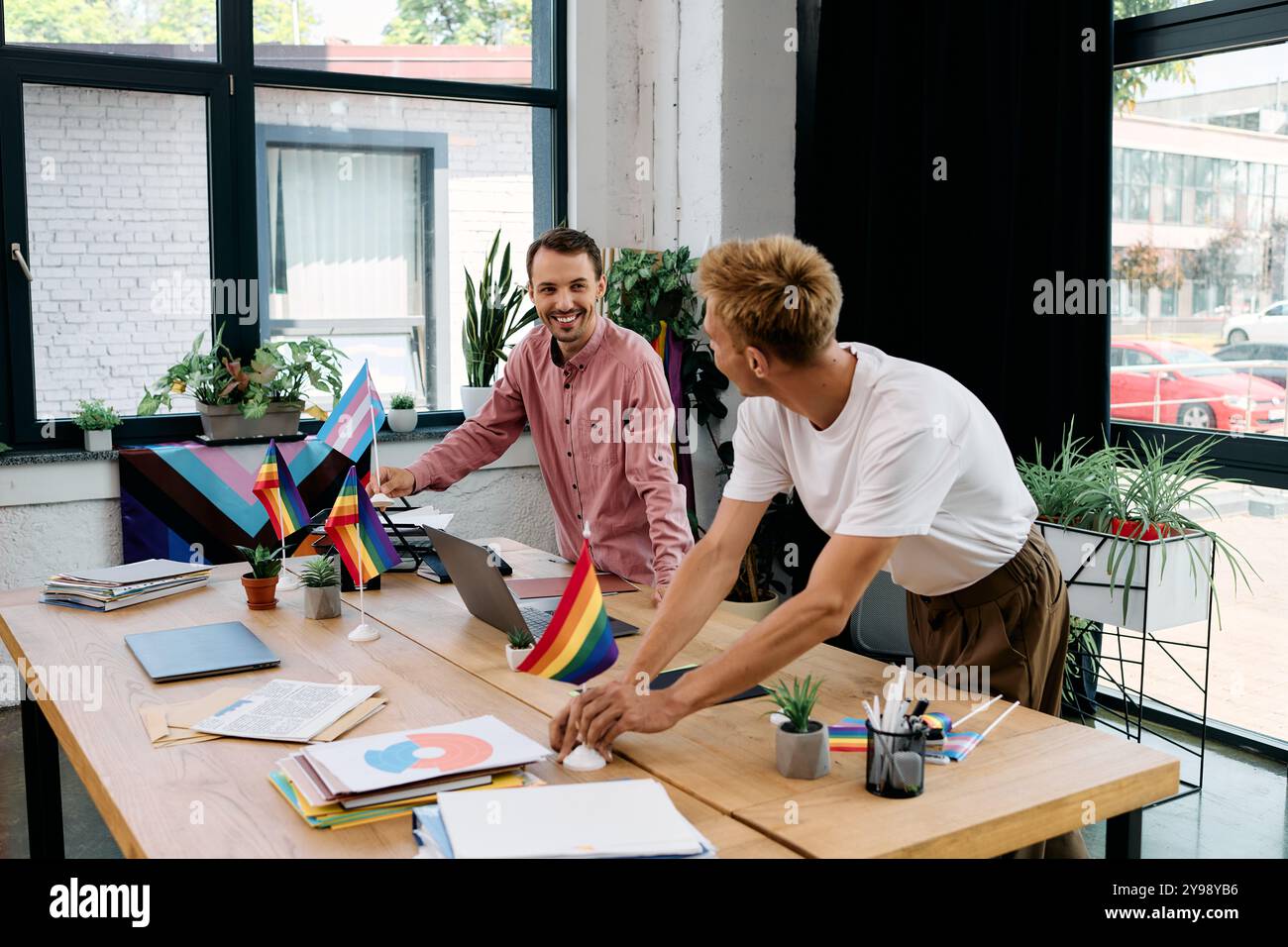 Two smiling men collaborate at a stylish desk adorned with pride flags ...