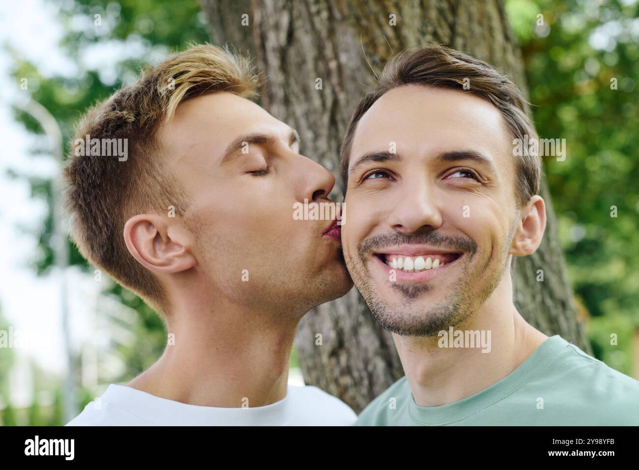 A charming couple shares a sweet kiss in a lush green park, radiating ...