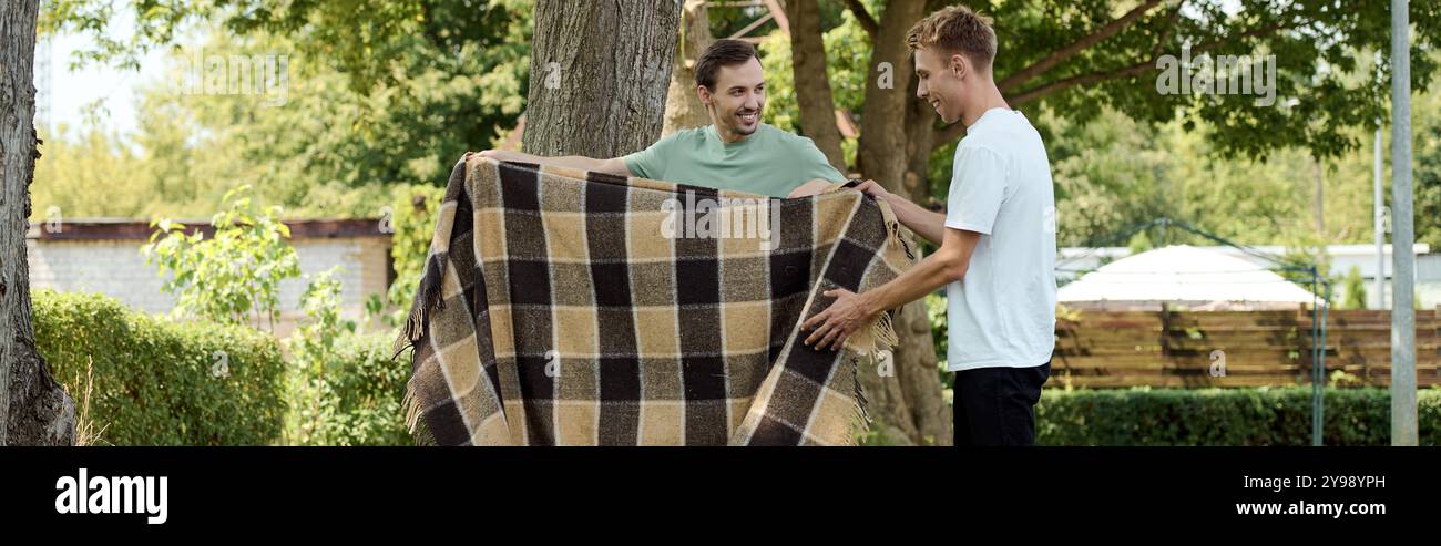 Two smiling men share a light moment as they arrange a blanket in a ...