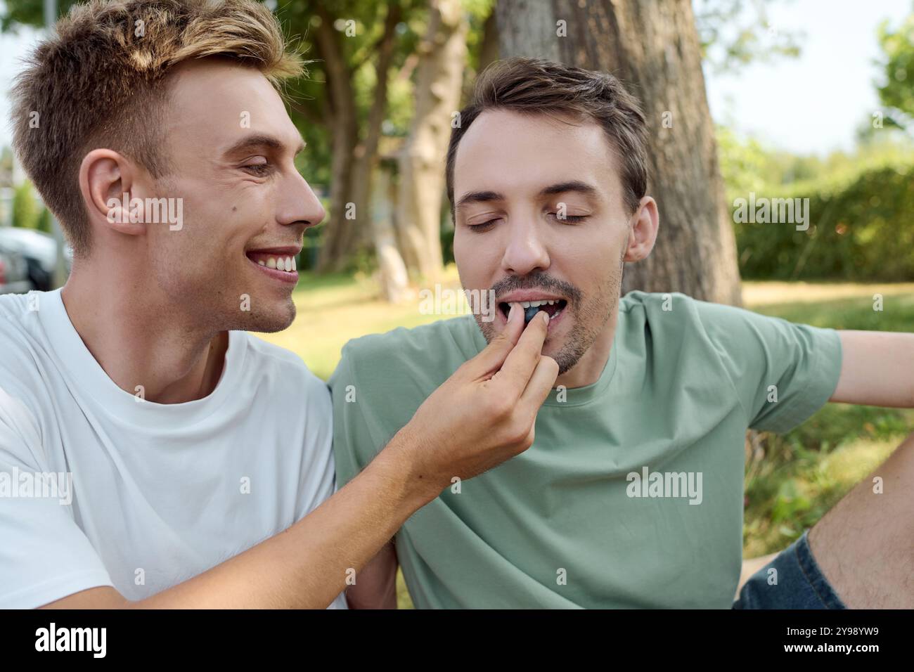 Two smiling men enjoy a playful moment while feeding each other ...