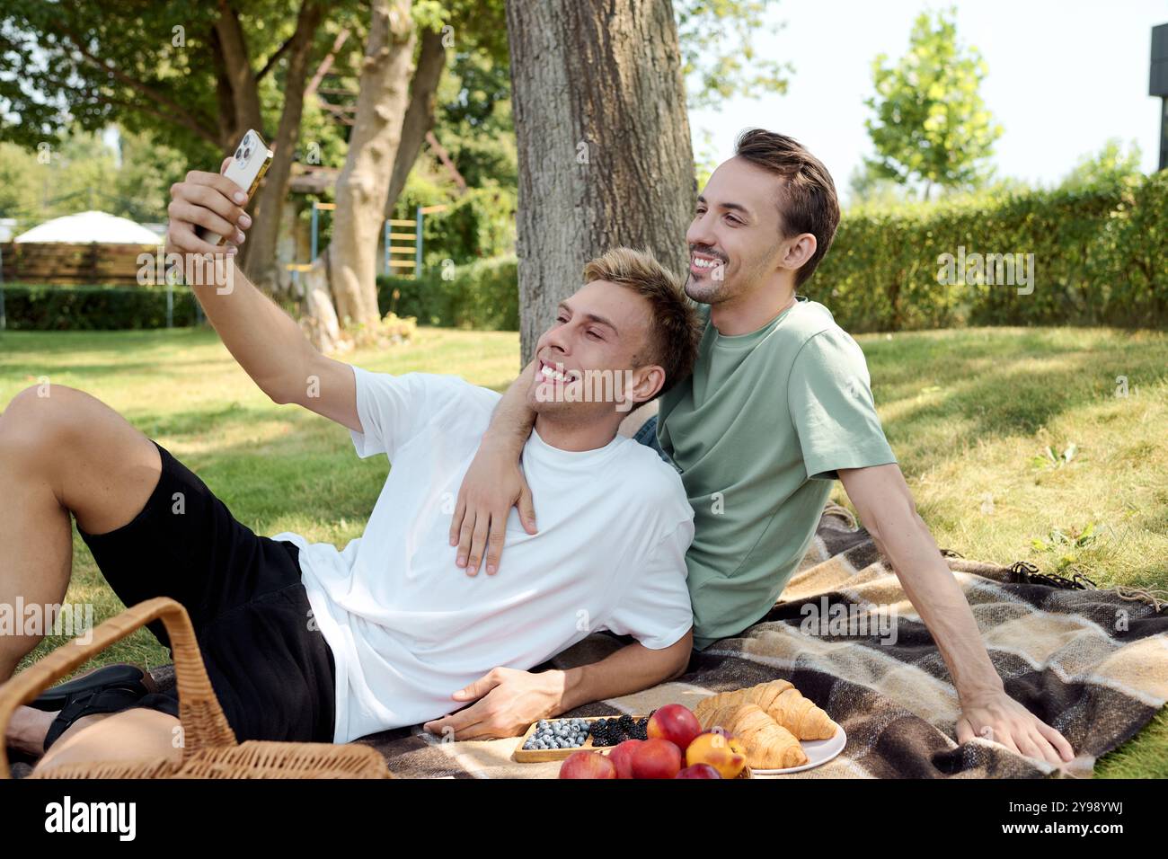 Two men enjoy a delightful picnic, smiling while taking a selfie ...