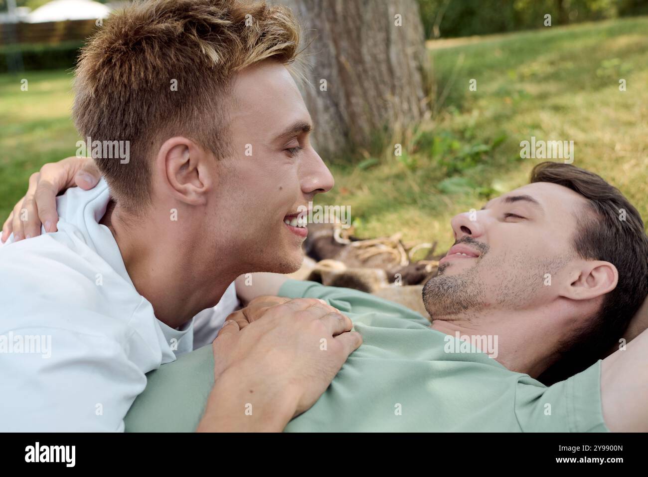 Two handsome men share a joyful moment in a lush green park, basking in ...