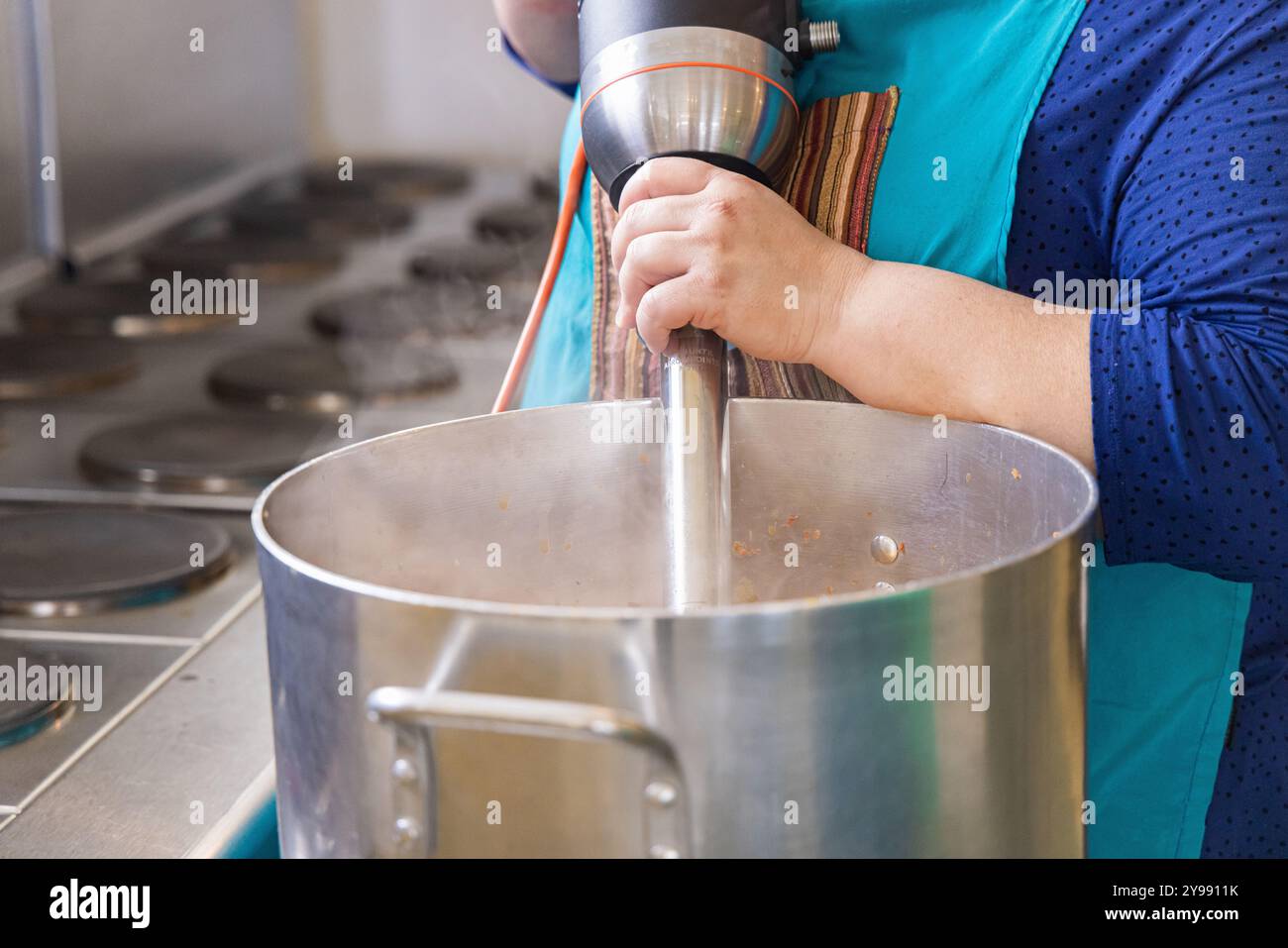 Cook is using an immersion blender while preparing a large amount of ...