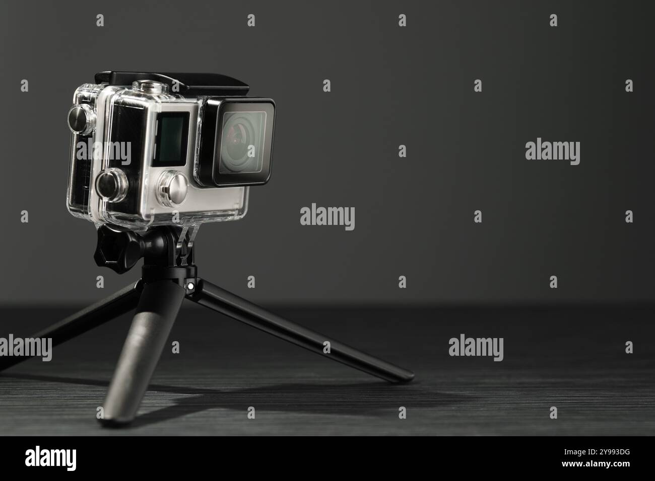 Modern action camera and tripod on grey wooden table. Space for text ...