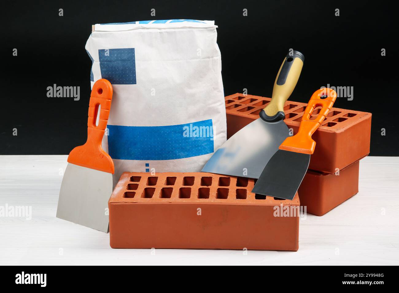 Cement powder in bag, putty knives and red bricks on white wooden table ...