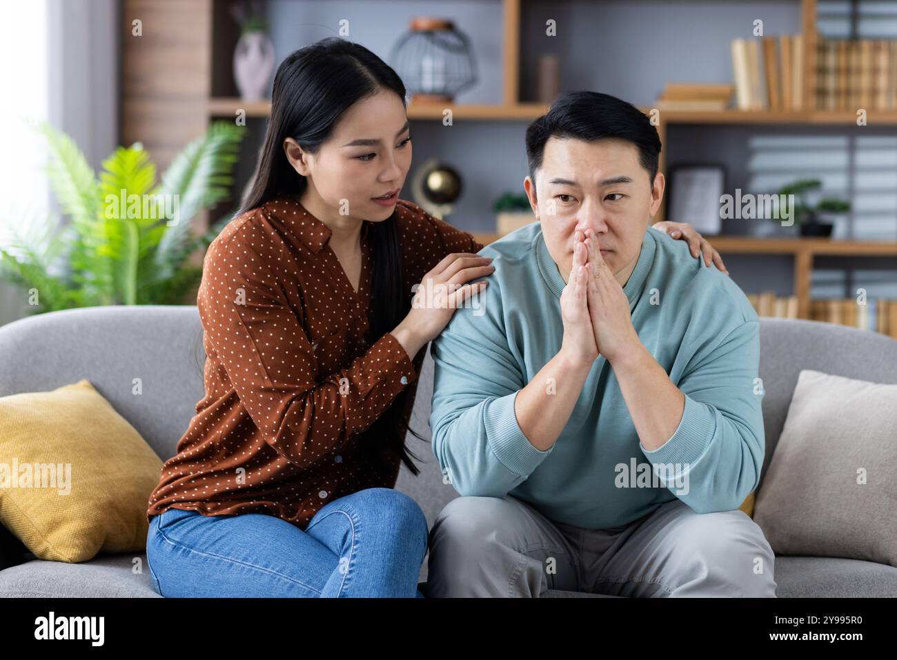 Asian couple sitting on sofa, woman comforting man, showing support ...