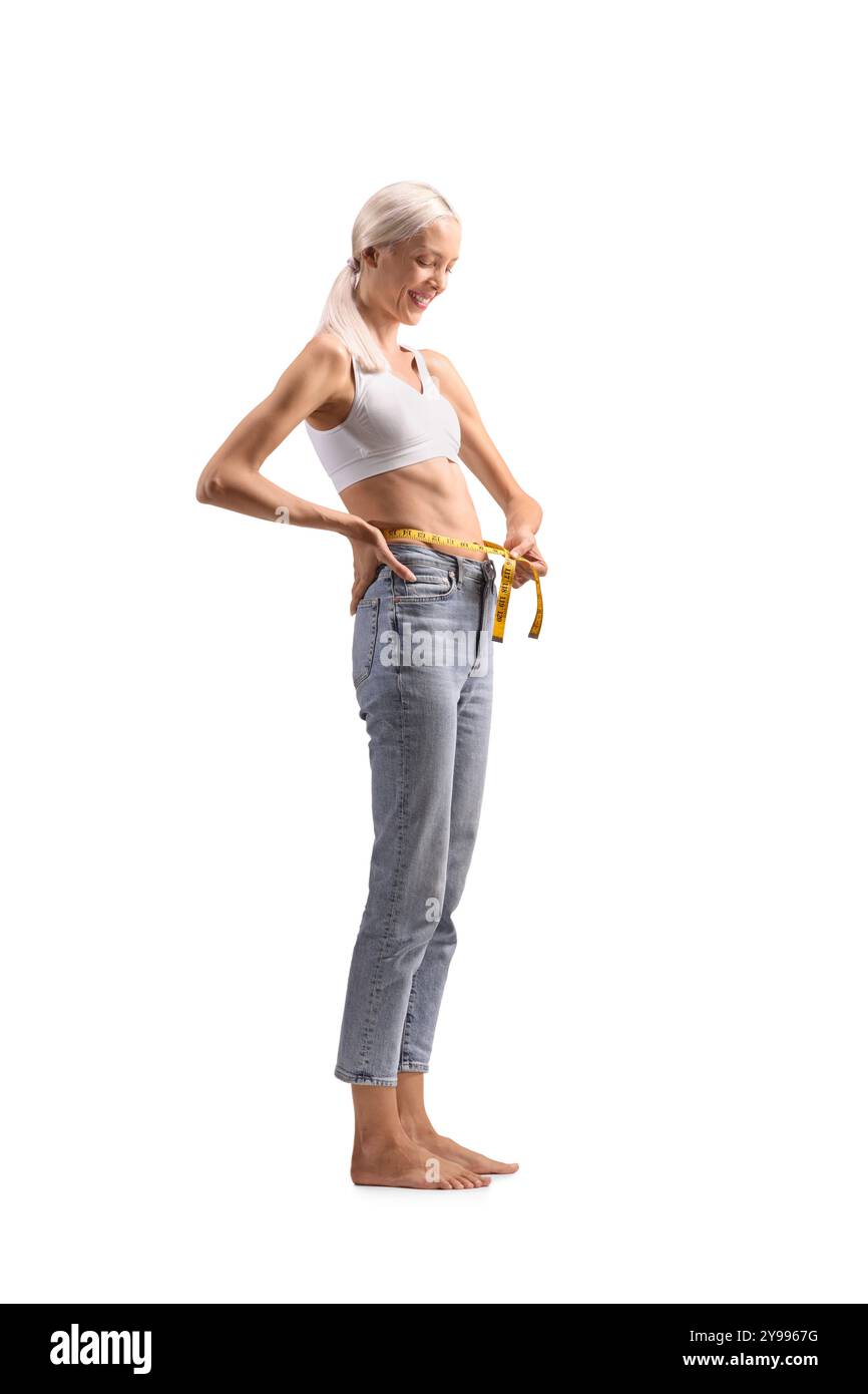Happy slim woman in jeans and crop top measuring waste with a tape ...