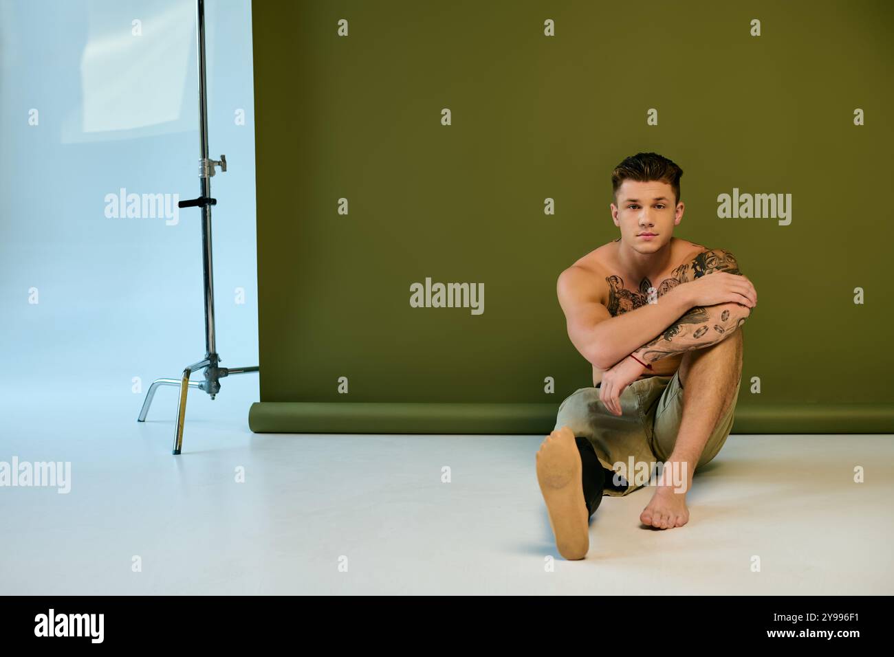 A young man with stunning tattoos sits confidently on the studio floor ...