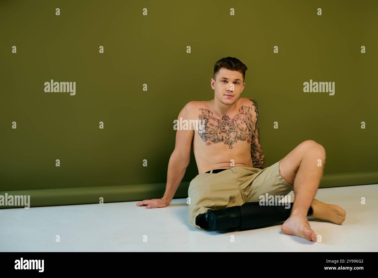 A young man with intricate tattoos sits on the floor, showcasing his ...