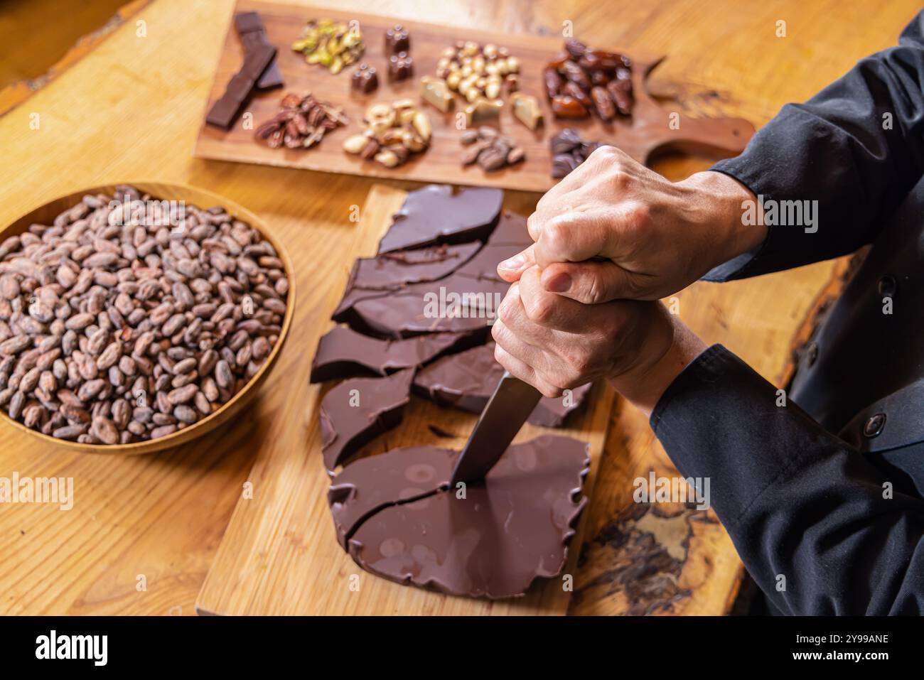 Chocolatier breaking a chocolate bar with a knife, surrounded by ...