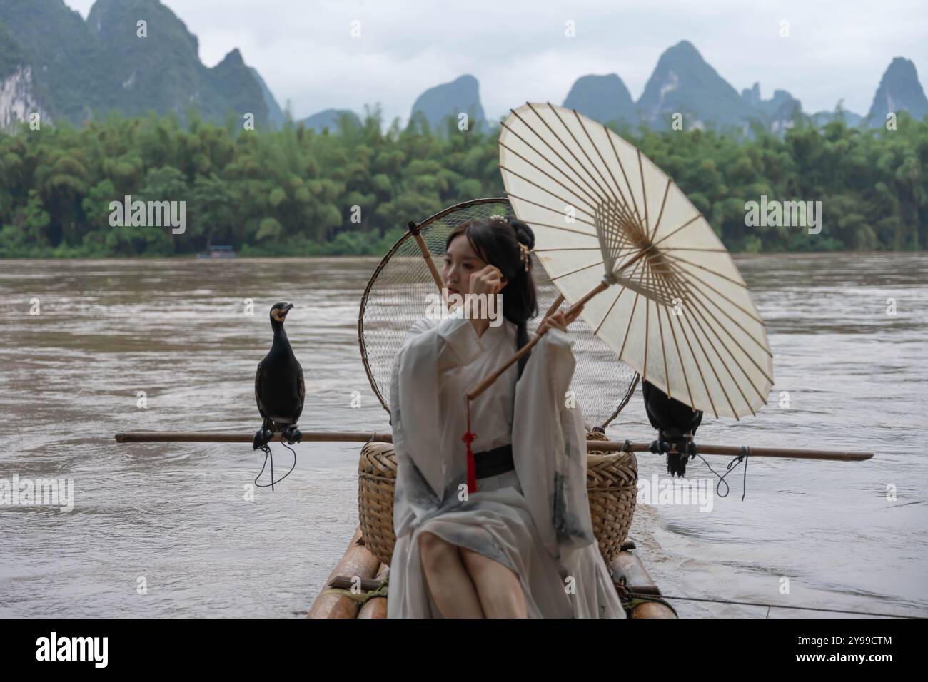 Hanfu girl fixing her hair and holding parasol while standing on bamboo ...