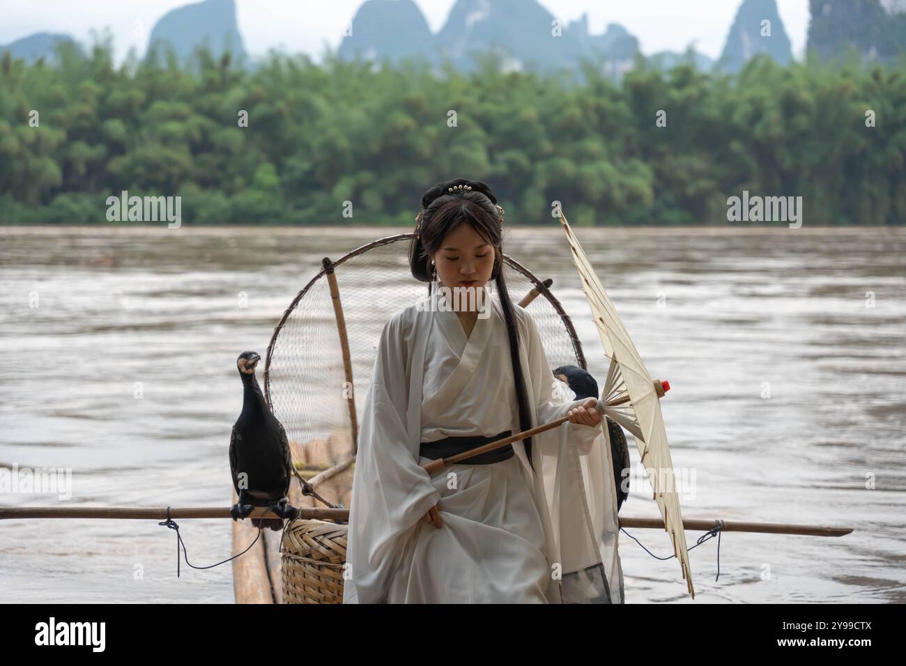 Chinese Hanfu girl with umbrella openning arms on bamboo raft in Li ...