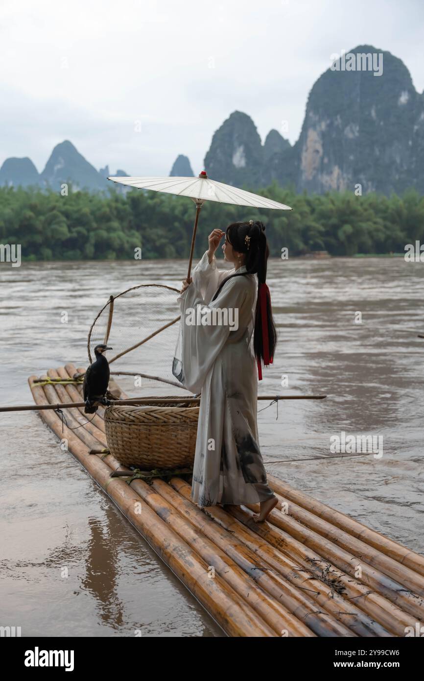 Woman in Hanfu attire holds an umbrella while standing on a bamboo raft ...